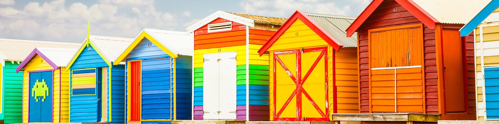 Bungalôs coloridos na praia com areia e céu claro.