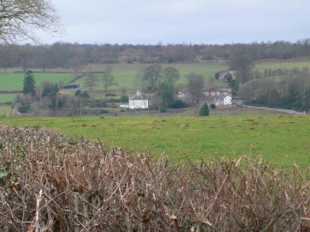 Paisagem rural com colinas onduladas, uma casa branca e um campo.