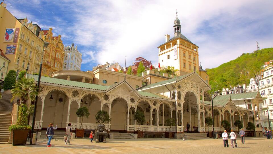 Um edifício histórico com arquitetura ornamentada, uma torre imponente e uma praça ao redor com pessoas e árvores.