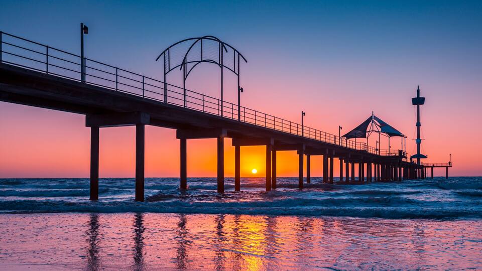 Um cais se estendendo para o oceano ao pôr do sol, com um céu claro acima.