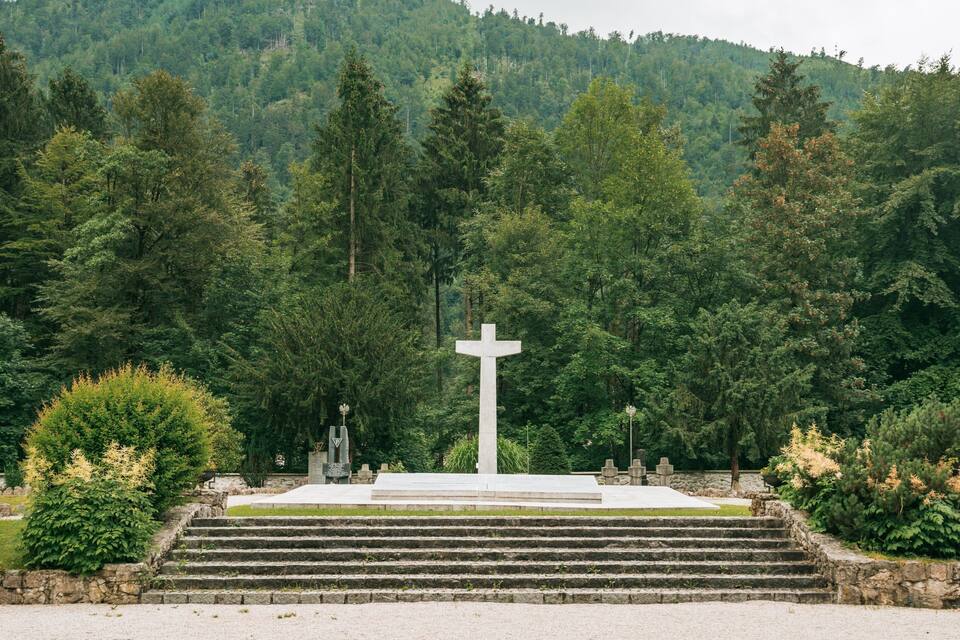 Um monumento em forma de cruz rodeado por degraus de pedra e uma floresta densa.