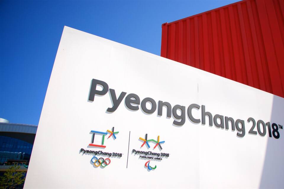 Placa dos Jogos Paralímpicos de PyeongChang 2018, com os anéis olímpicos e um logotipo estilizado de avião.