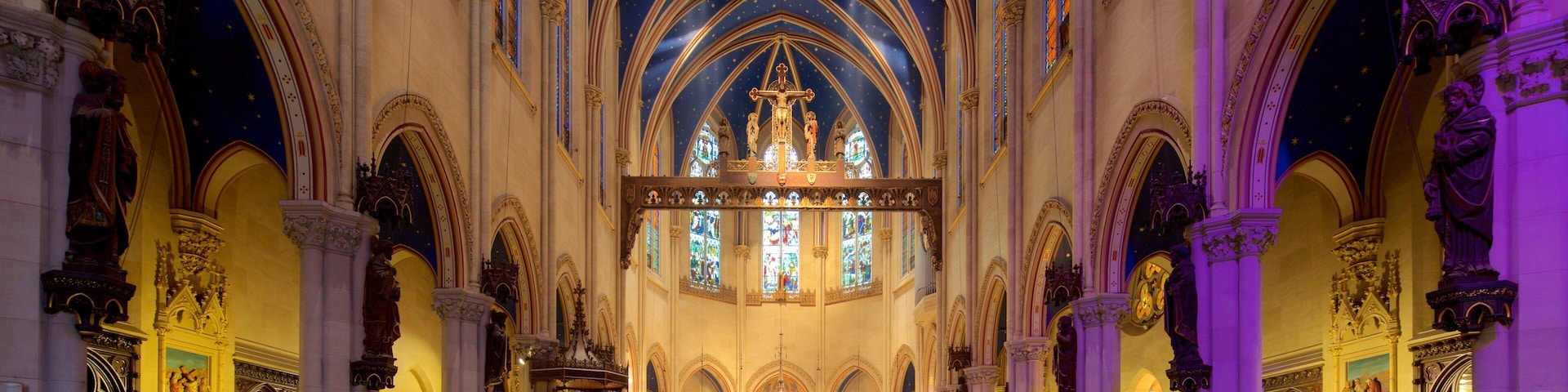 Interior de uma catedral com altos tetos abobadados, janelas de vitrais e fileiras de bancos.