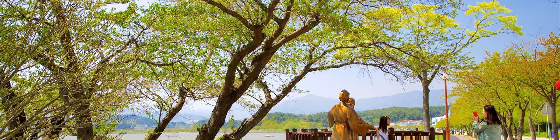 Um parque com uma estátua, um lago e árvores.