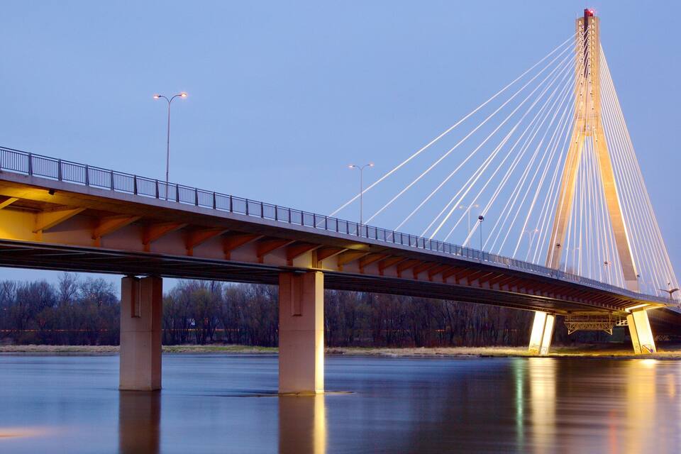 Uma ponte atirantada com uma passarela iluminada e um rio abaixo.