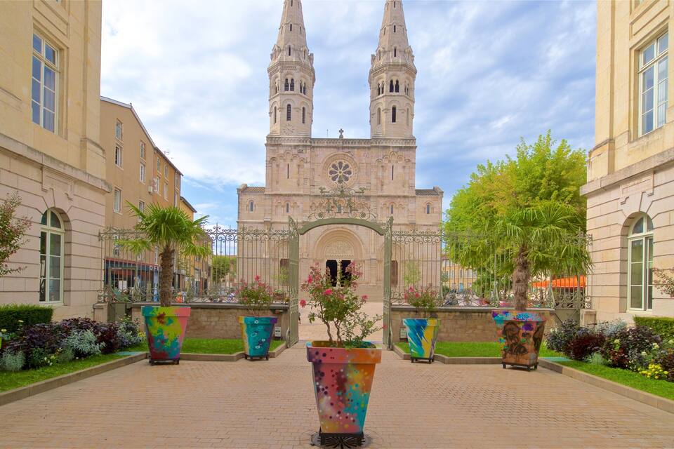 Uma igreja histórica com duas torres e um arco central, rodeada por caminhos de tijolos e vasos coloridos.