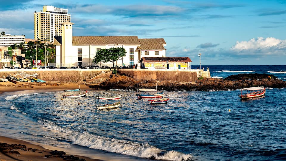 Uma vila costeira com praia, barcos e um edifício alto.