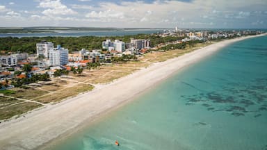 Paisagem costeira urbana com uma extensa praia arenosa, águas turquesa cristalinas e uma combinação de edifícios residenciais e comerciais.