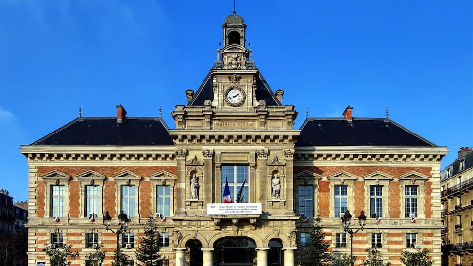 Um edifício histórico com torre do relógio, colunas e bandeiras.