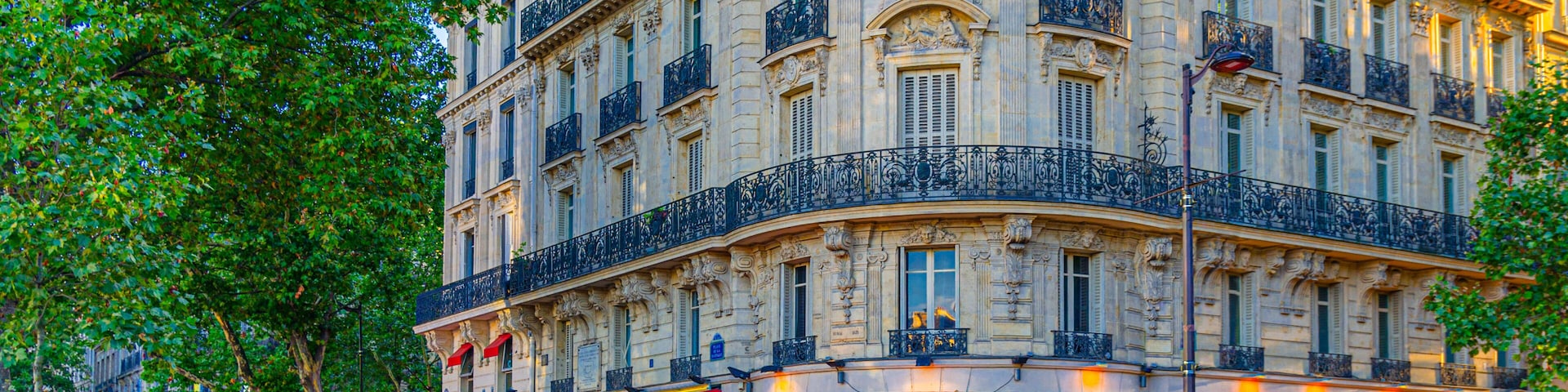 Um edifício histórico parisiense com varandas elaboradas e toldos vermelhos.