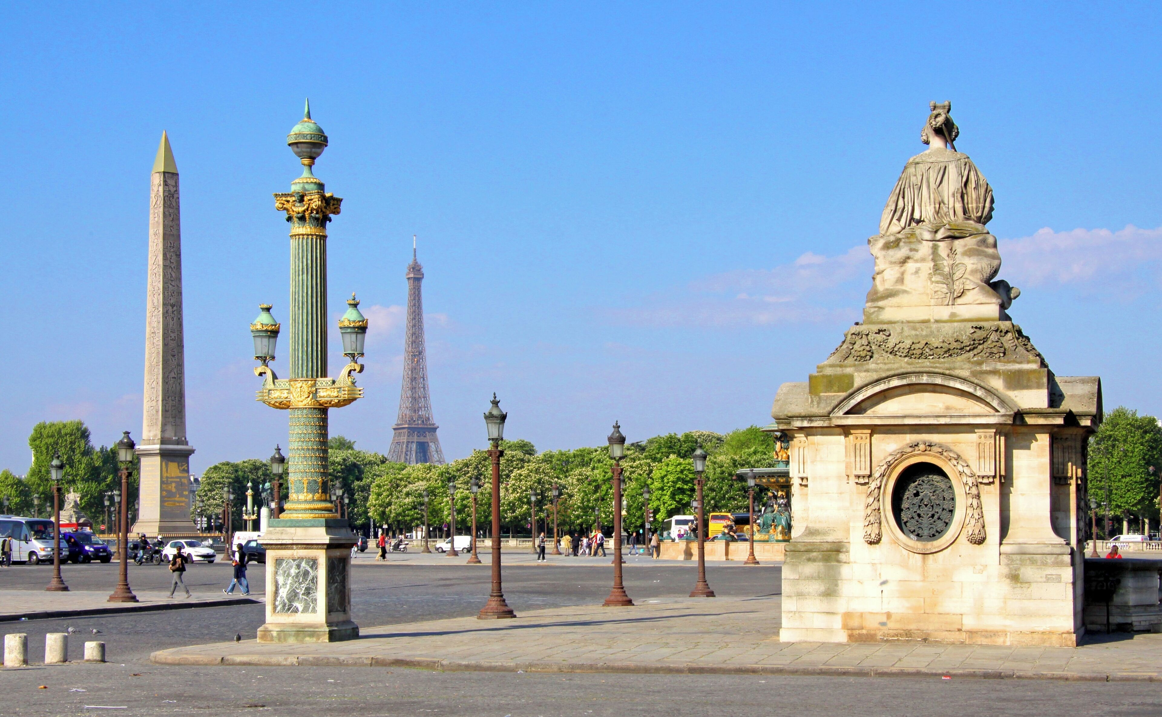 Um monumento com uma estátua, um obelisco alto e a Torre Eiffel ao fundo.
