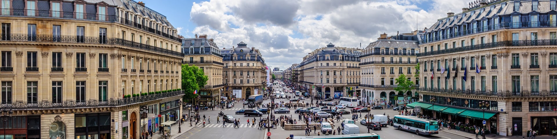 Uma rua movimentada em Paris, com edifícios históricos, uma faixa de pedestres e um ônibus verde.