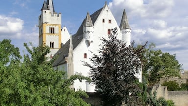 Um castelo branco com várias torres e uma torre do relógio, rodeado por vegetação.