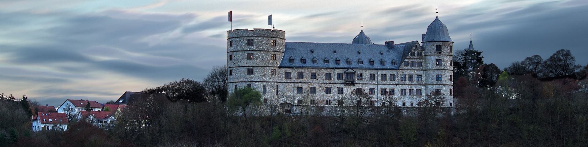 Um castelo de pedra imponente com várias torres e uma colina íngreme em primeiro plano.