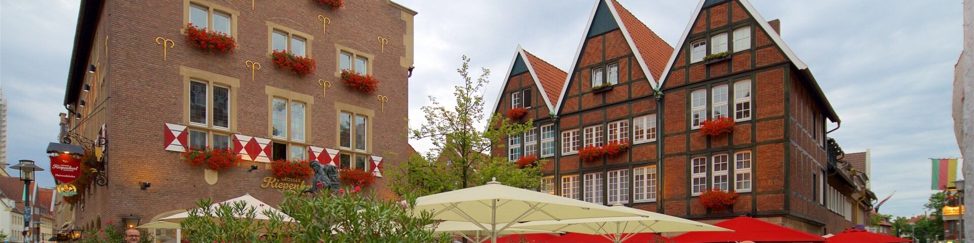 Um café ao ar livre movimentado, com clientes sentados em mesas, rodeado por arquitetura europeia tradicional.