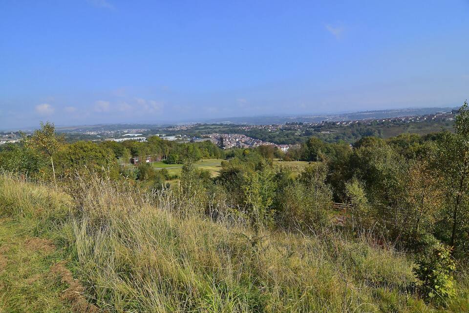 Vista panorâmica de uma cidade aninhada num vale, rodeada por vegetação exuberante e colinas ondulantes.