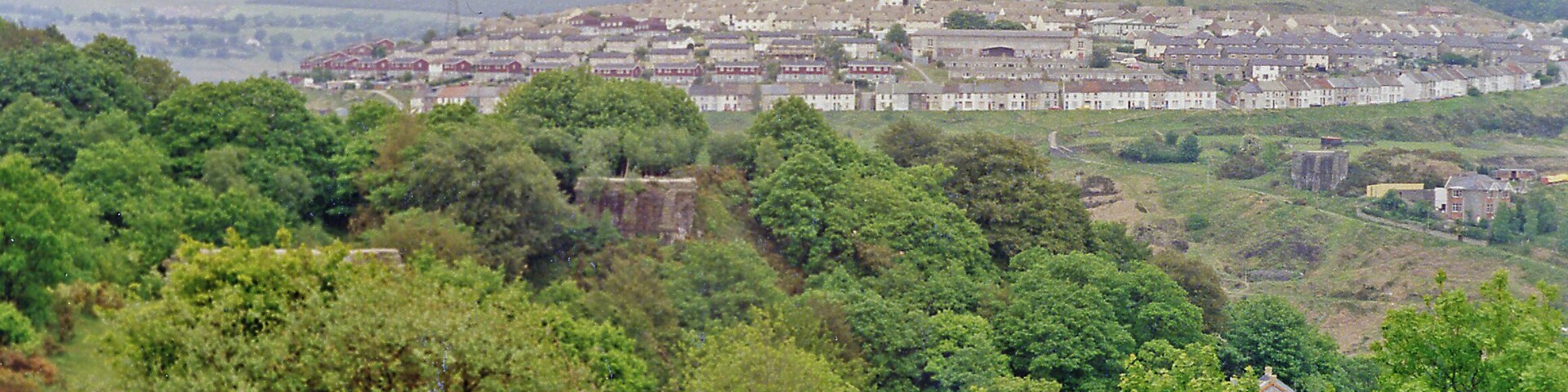 Northward in Ebbw Valley at site of Crumlin Viaduct, 1990. View NW to Swffryd, probably from the A472 road, over the site of the former Crumlin Viaduct, some residual piers of which can be seen. Demolished in 1967, the viaduct carried the ex-GW Pontypool Road (to the right) - Aberdare - Neath line, which was closed on 15/6/64, across the valley and the Newport - Ebbw Vale/Brynmawr line at Crumlin (Low Level)
