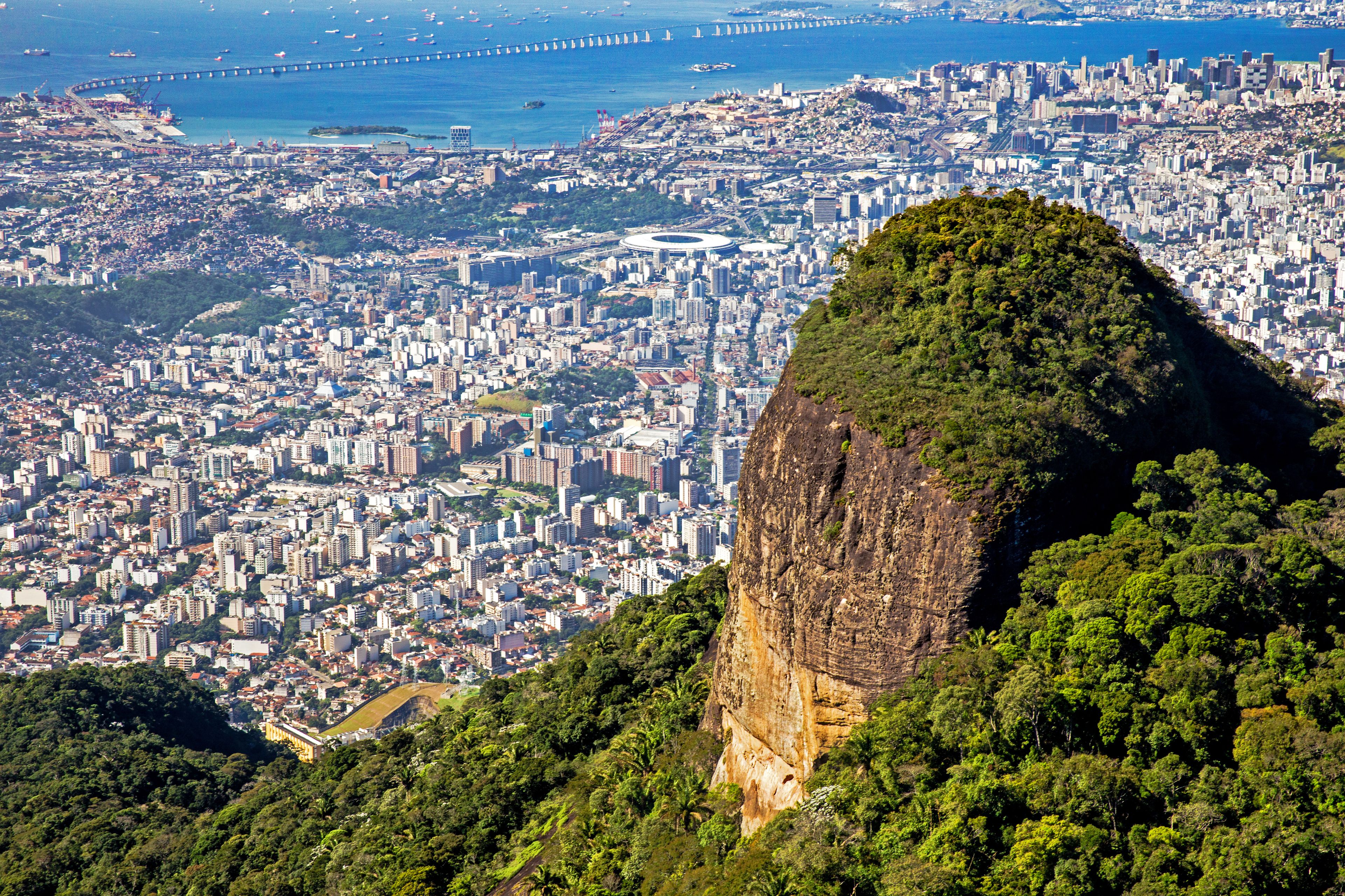 Paisagem urbana com um pico de montanha em destaque ao primeiro plano e uma ponte ao fundo.
