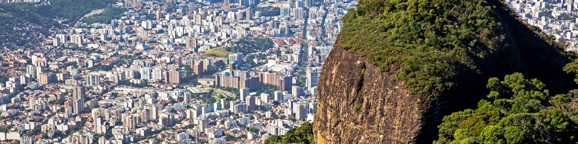 Paisagem urbana com um pico de montanha em destaque ao primeiro plano e uma ponte ao fundo.