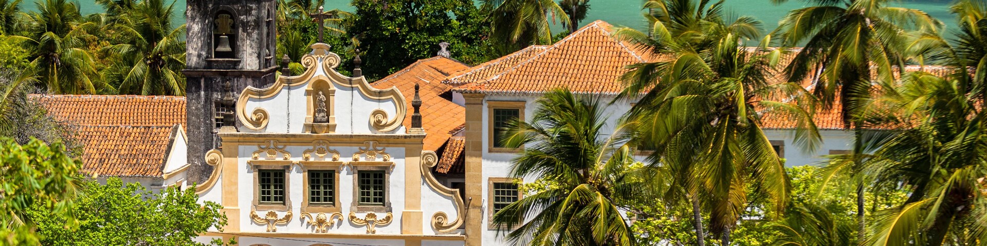 Uma vila costeira com uma igreja imponente, palmeiras e uma vista clara do oceano.
