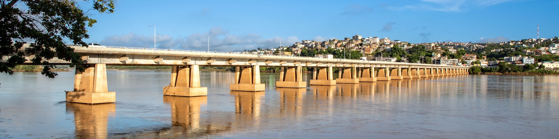 Uma ponte sobre um rio calmo, com um horizonte urbano ao fundo.