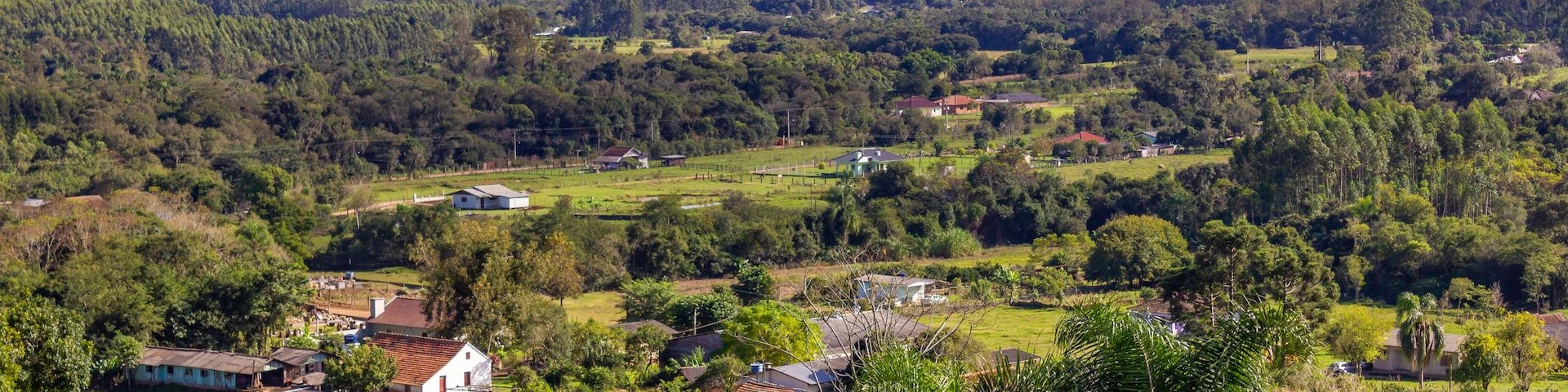 Paisagem rural com colinas ondulantes, casas dispersas e vegetação verde exuberante.