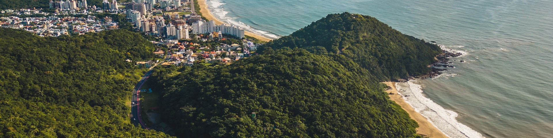 Uma cidade costeira com intenso desenvolvimento urbano, uma estrada sinuosa e uma praia.