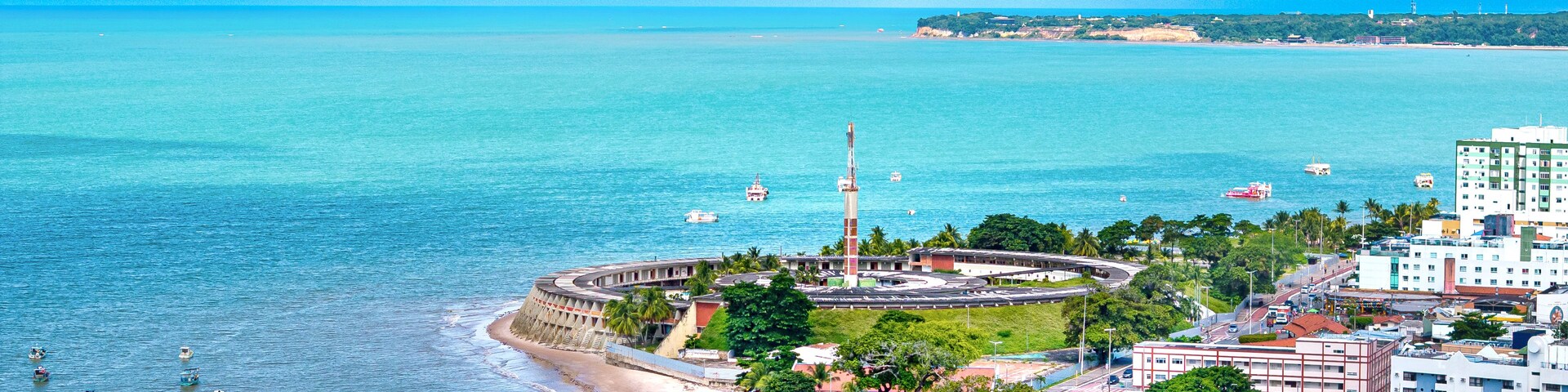 Paisagem costeira urbana com um farol imponente, praia e edifícios.