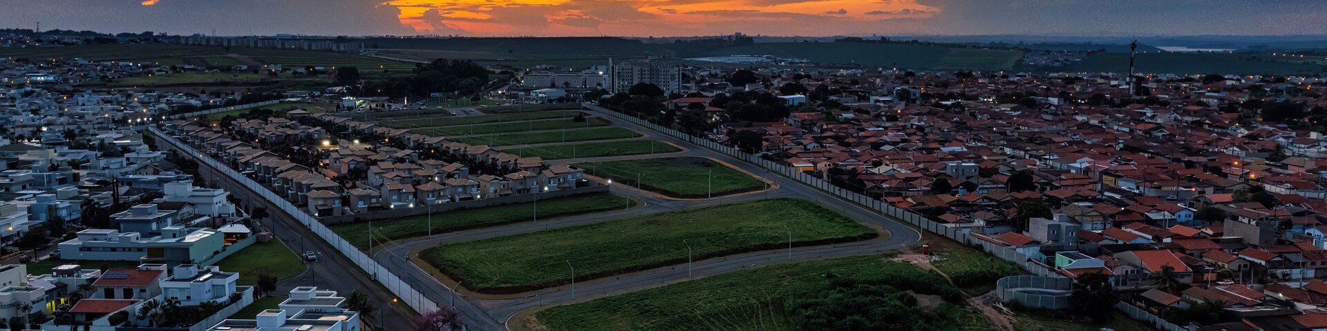 Zona residencial com casas, estrada e campos ao pôr do sol.