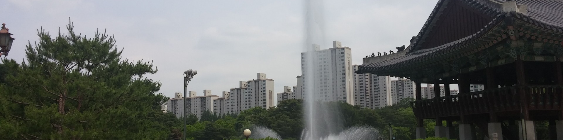 Um pavilhão tradicional, uma fonte e edifícios altos modernos ao fundo.