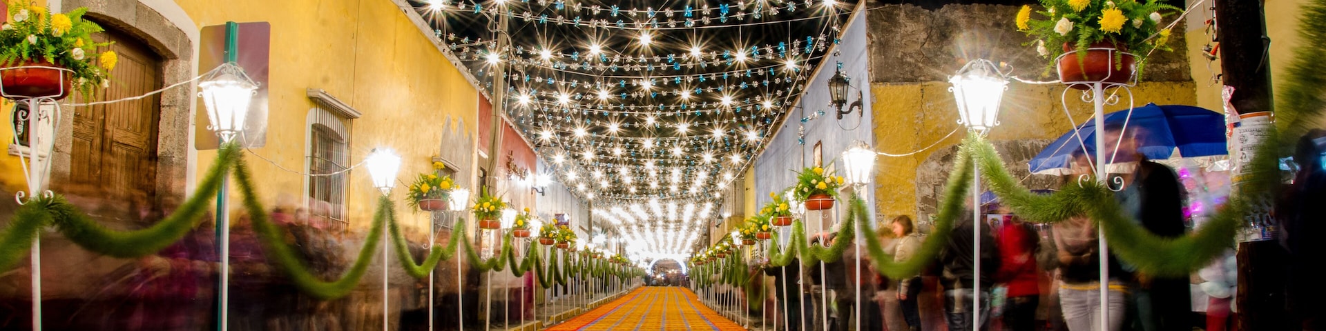 Uma rua decorada com tapete estampado, luzes de cordão e vegetação.