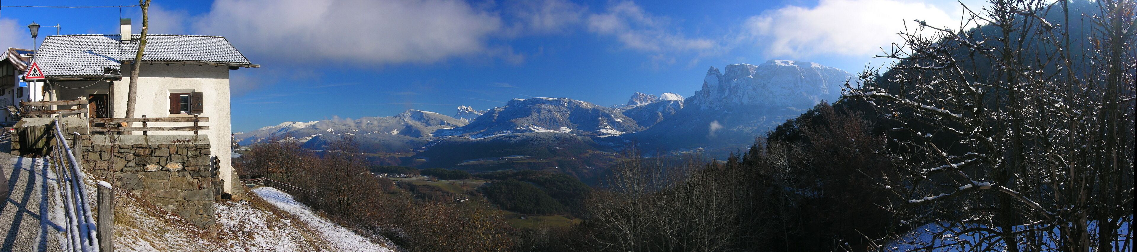 Paisagem montanhosa com picos nevados, um edifício de pedra e céu azul límpido.