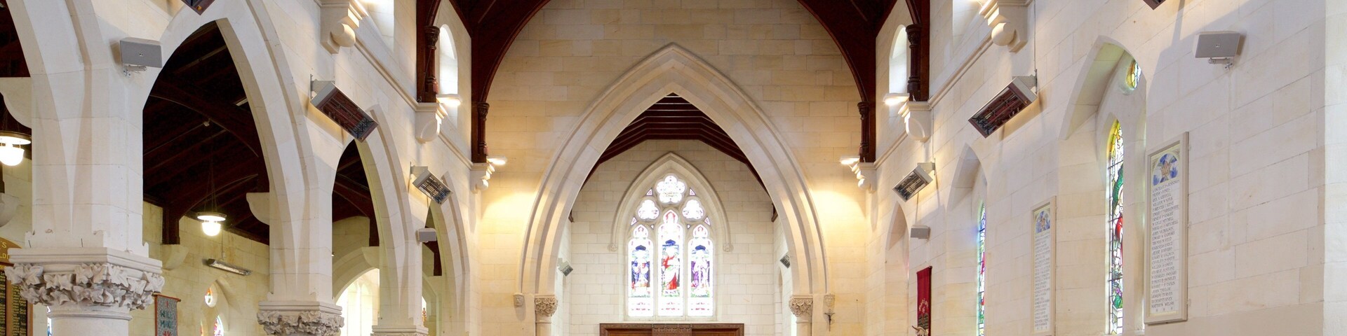 Interior de igreja com bancos de madeira, tapete vermelho e vitrais.