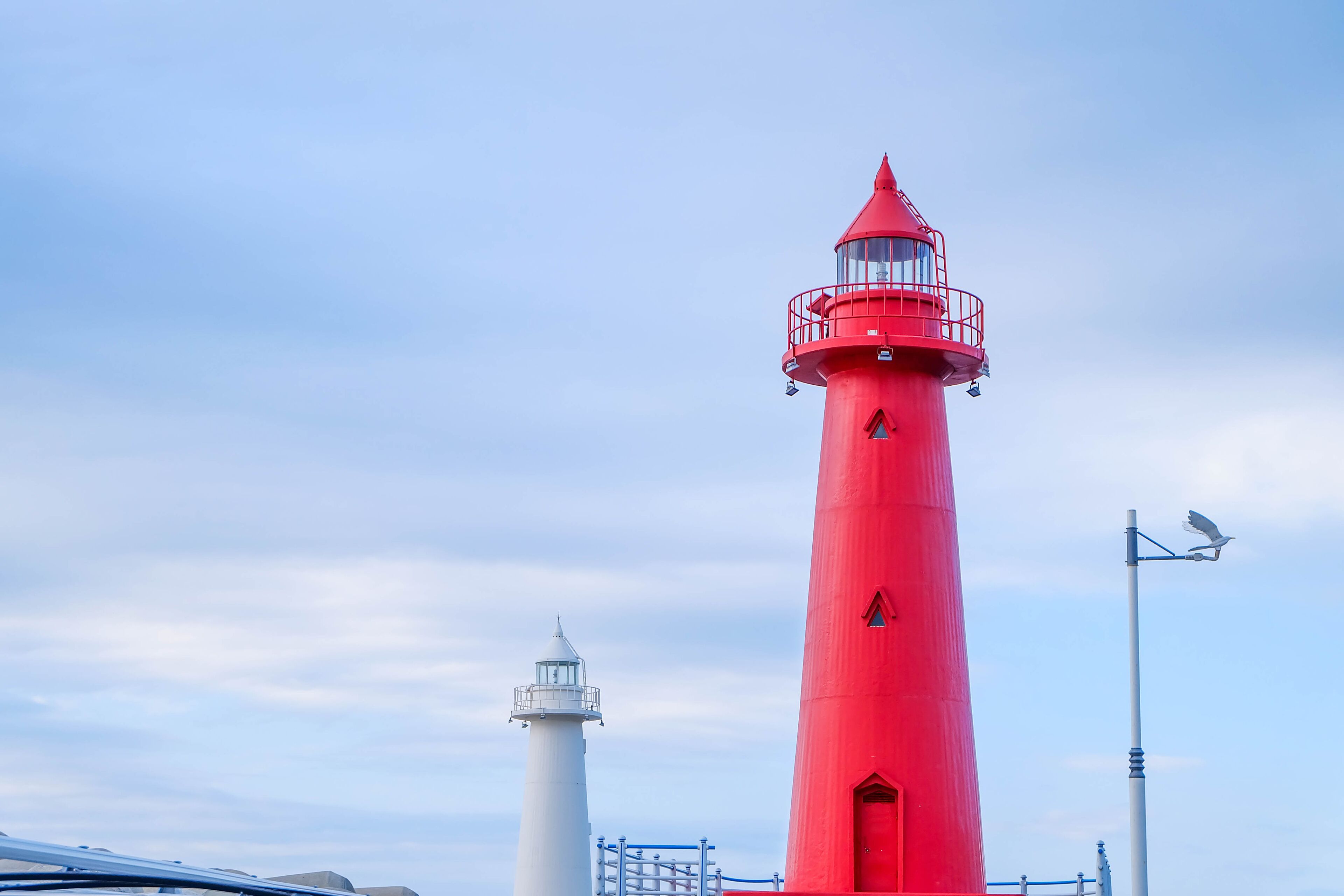 Um farol vermelho com uma torre branca ao fundo.