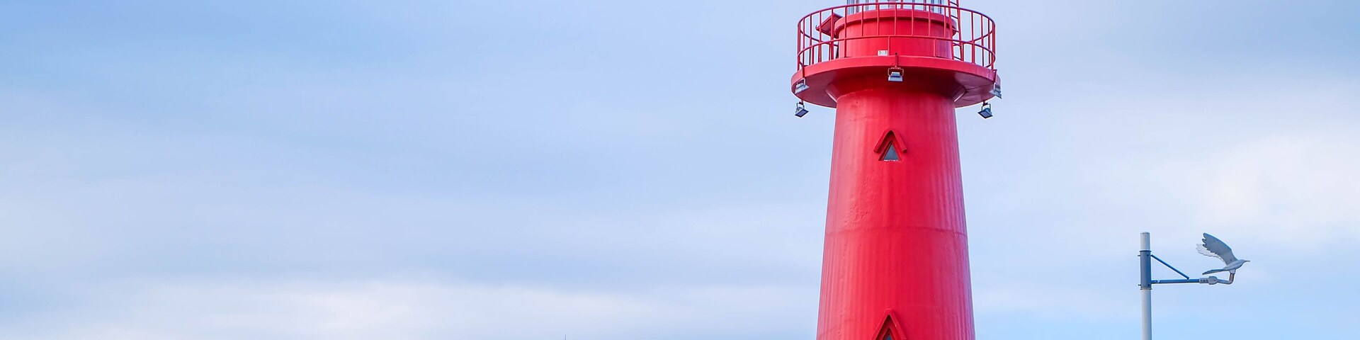 Um farol vermelho com uma torre branca ao fundo.