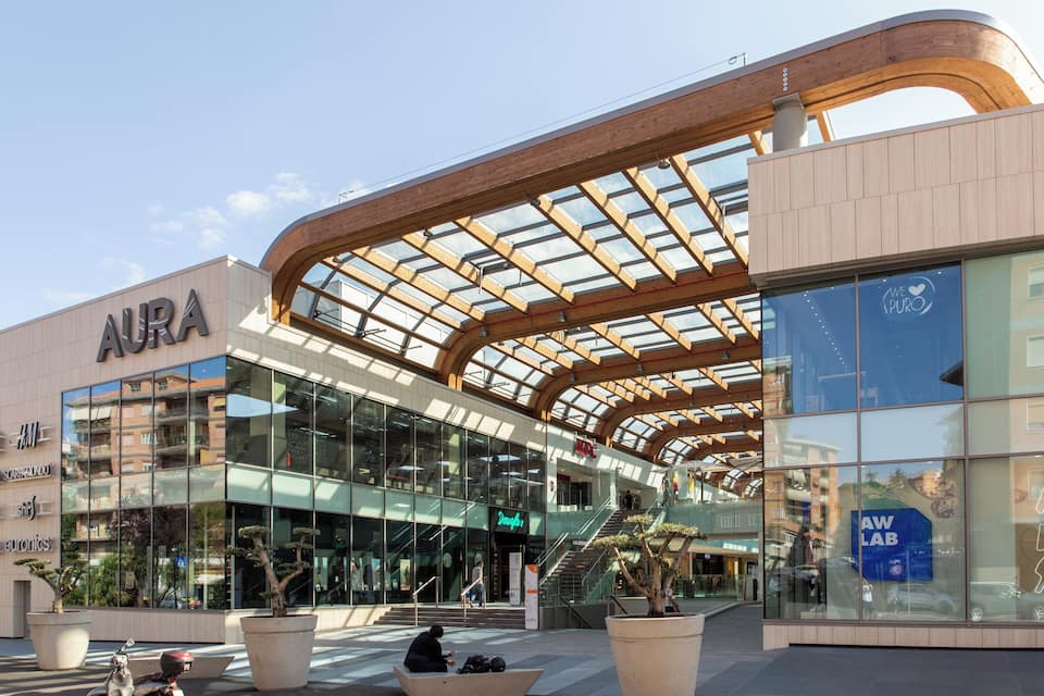 Um shopping moderno com fachada de vidro e estrutura de telhado em madeira.
