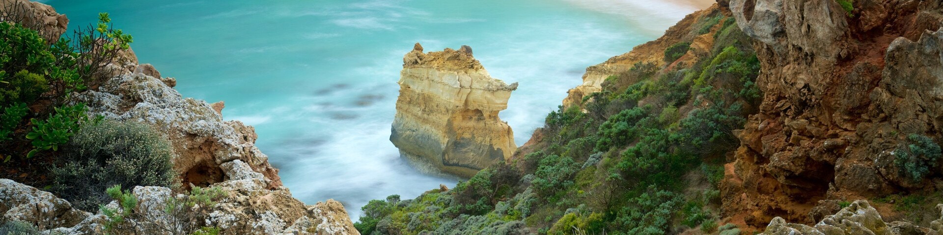 Paisagem costeira com praia arenosa, águas azul-turquesa e falésias rochosas.