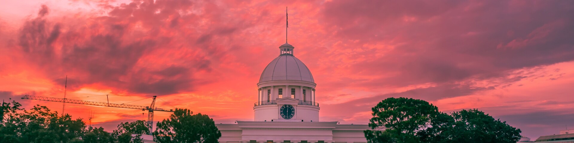 Um edifício grande e branco com cúpula e colunas, cercado por árvores e um céu ao entardecer.