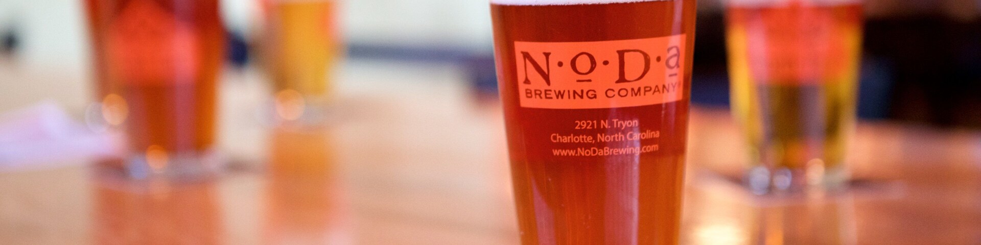 Um copo de cerveja com etiqueta que diz 'N.O.D. Brewing Company' sobre uma mesa de madeira.