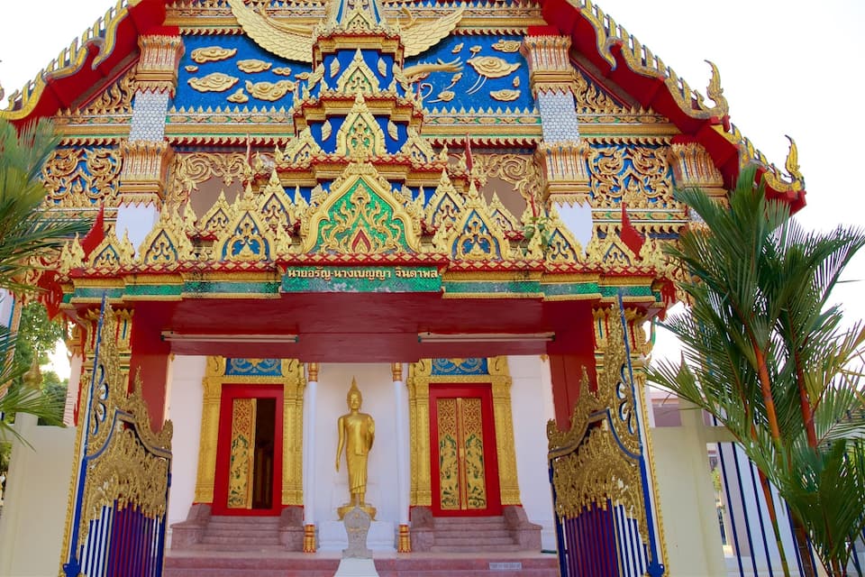 Um templo com decorações douradas e azuis detalhadas, uma estátua central de Buda e uma entrada vermelha e branca.