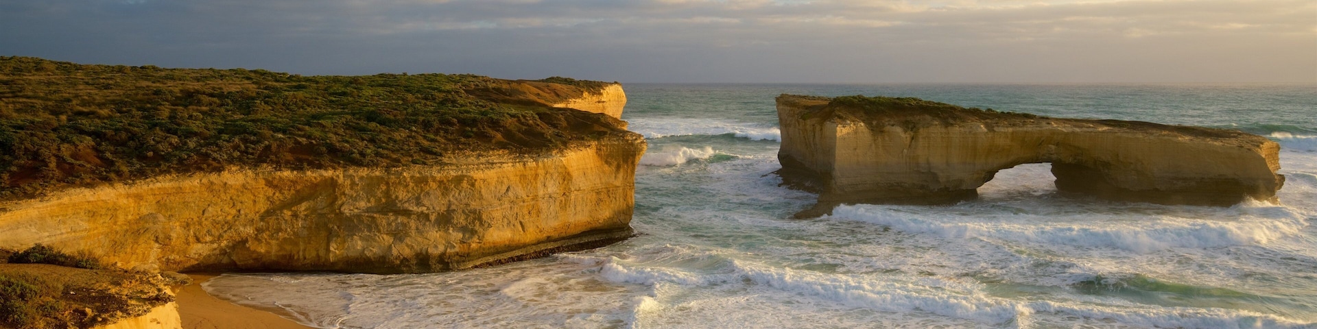Paisagem costeira com falésias e um arco natural no mar.