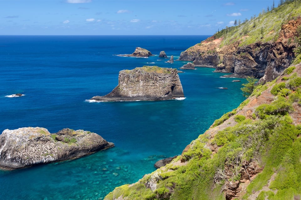 Paisagem costeira com águas azul-claras, afloramentos rochosos e vegetação verde.