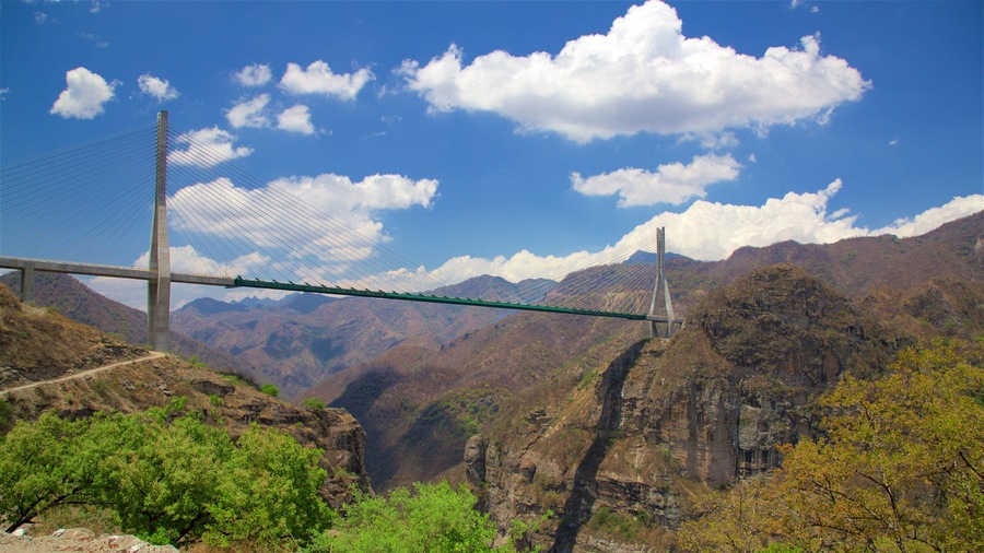 Uma ponte suspensa sobre um cânion, com montanhas ao fundo.