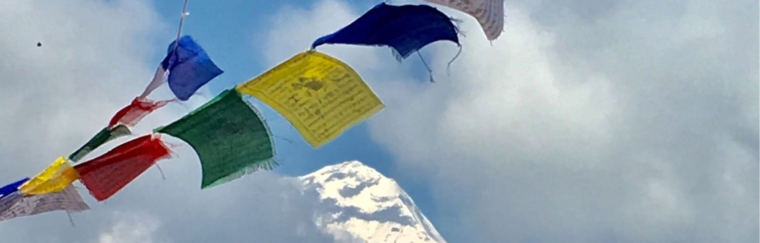 Bandeirinhas de oração penduradas sobre uma cordilheira com pico nevado ao fundo.