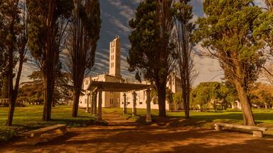 Um parque com um coreto, árvores e um edifício com uma torre do relógio.