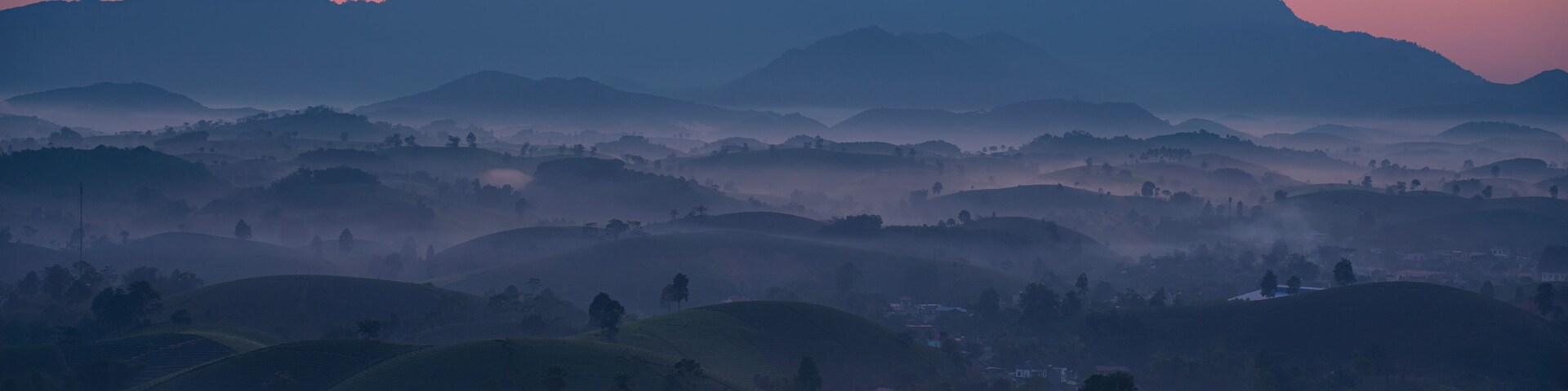 Paisagem montanhosa com colinas suaves e nascer ou pôr do sol.