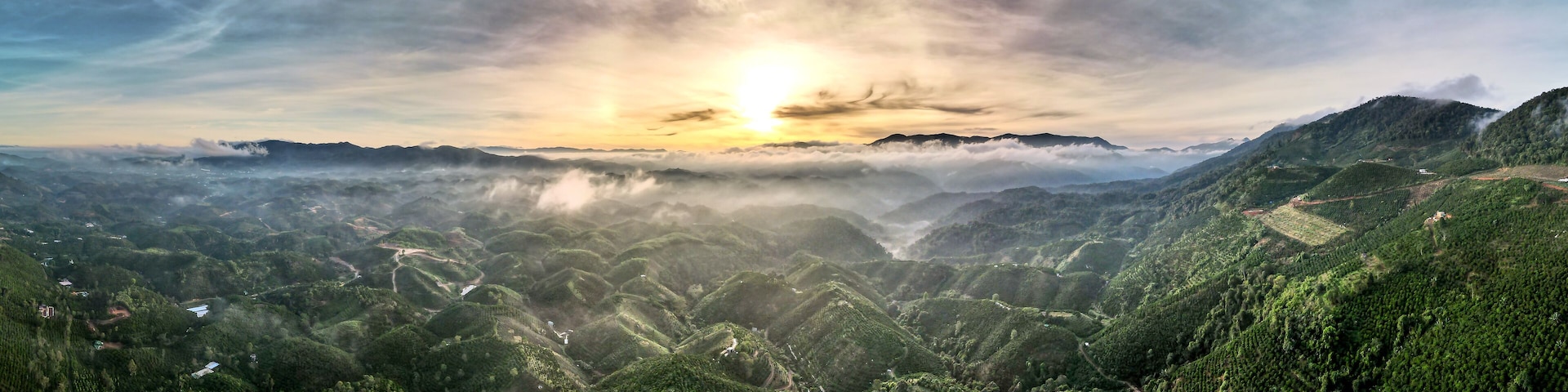 Paisagem montanhosa com nascer do sol, campos em socalcos e estrada sinuosa.