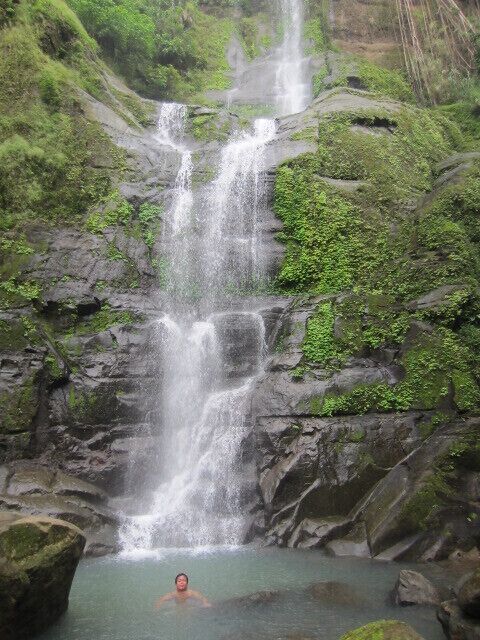 Uma cascata desce sobre rochas, rodeada por vegetação exuberante.
