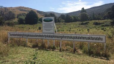Placa numa relva com montanhas ao fundo.