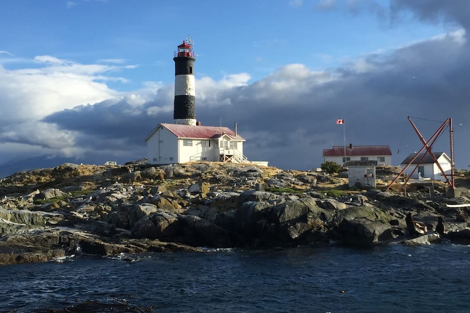Um farol numa costa rochosa com telhado vermelho, uma bandeira canadense e uma grua vermelha.